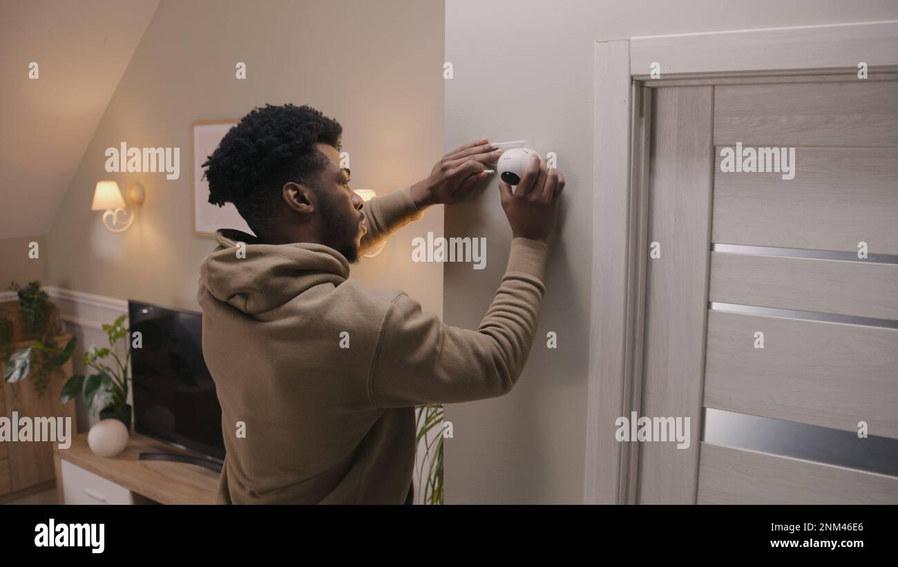 African American man puts security camera on wall fastening and ...
