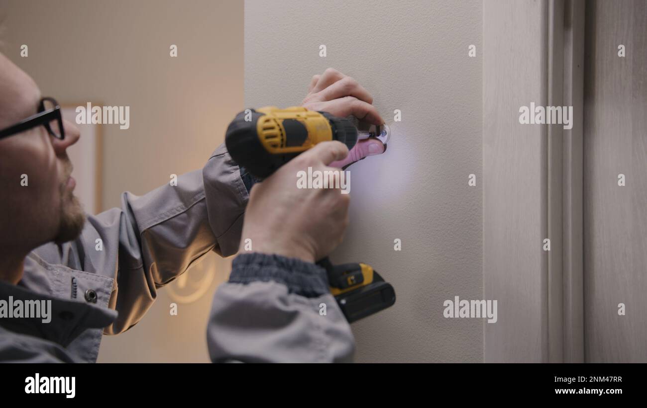 Man in uniform and glasses screws security camera mount into concrete ...