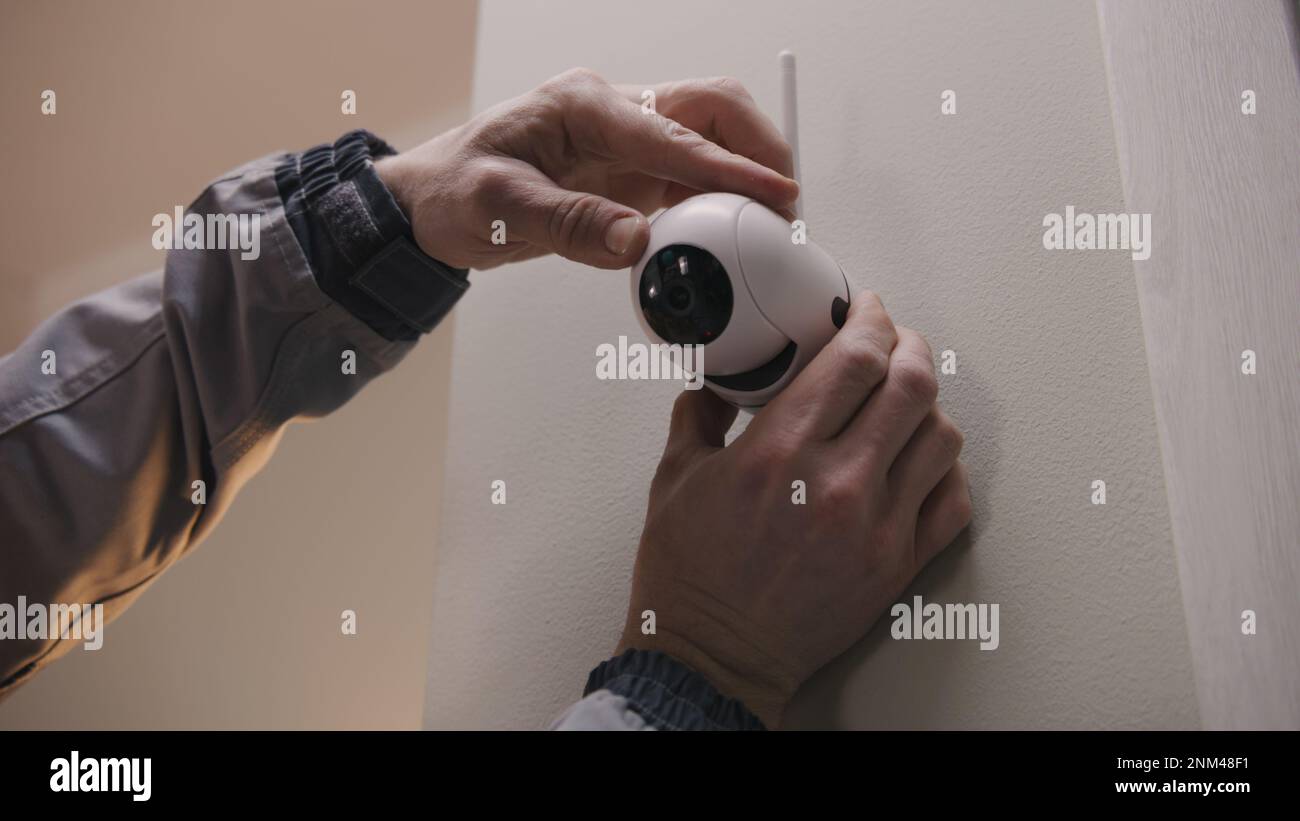 Installer in uniform puts security camera on wall fastening and ...