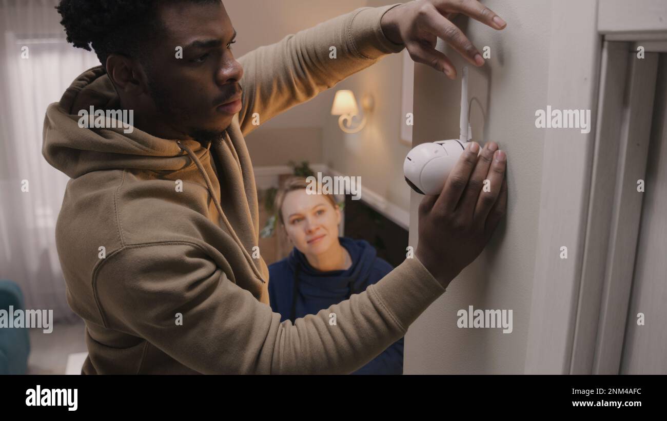 African American man connects security camera with wire and fastening ...