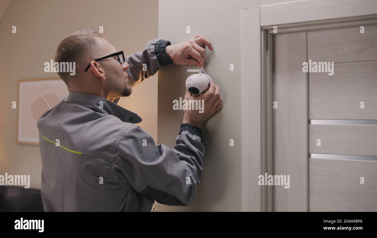 Installer in uniform puts security camera on wall fastening and ...