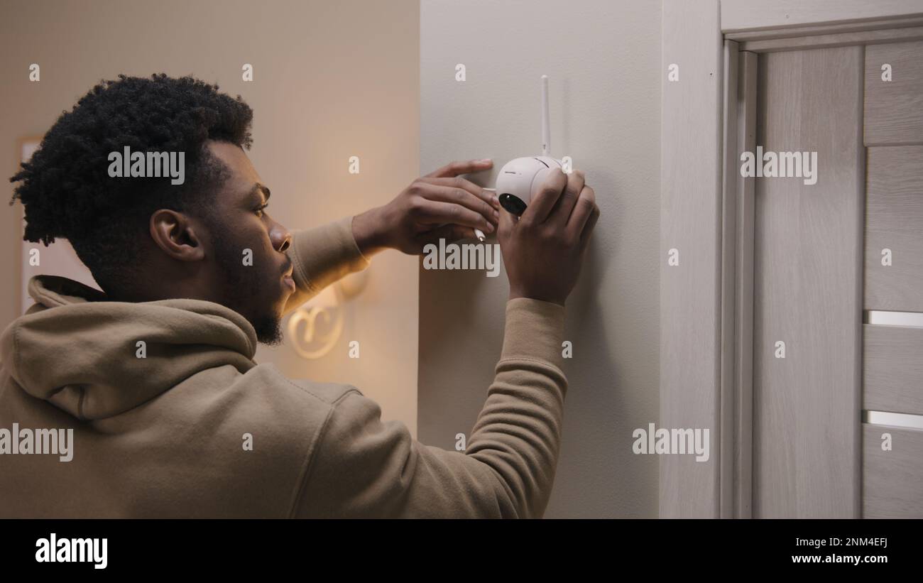 African American man puts security camera on wall fastening and ...