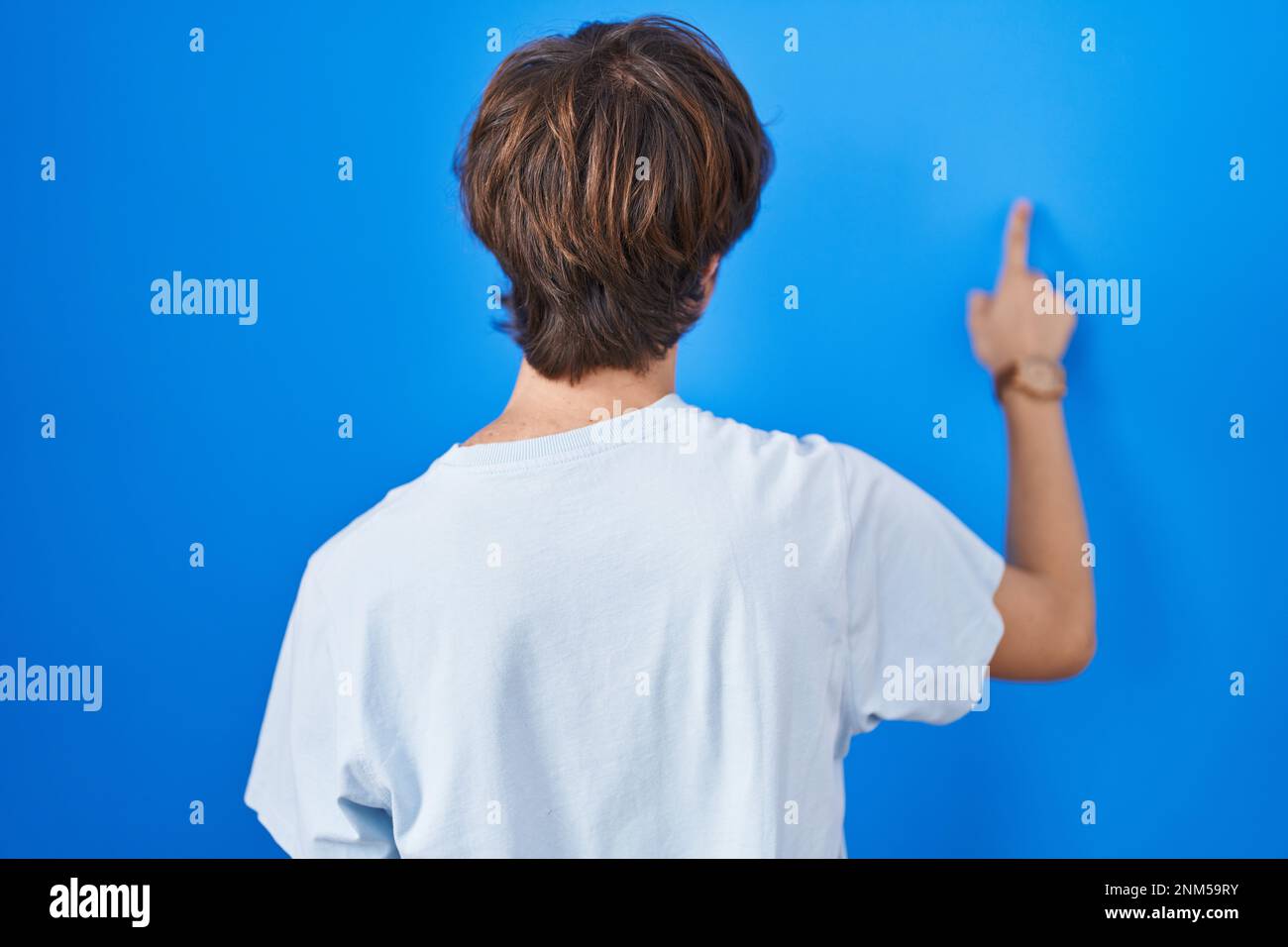 Hispanic young man standing over blue background posing backwards ...