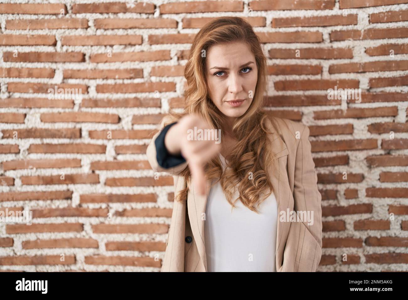 Beautiful Blonde Woman Standing Over Bricks Wall Looking Unhappy And