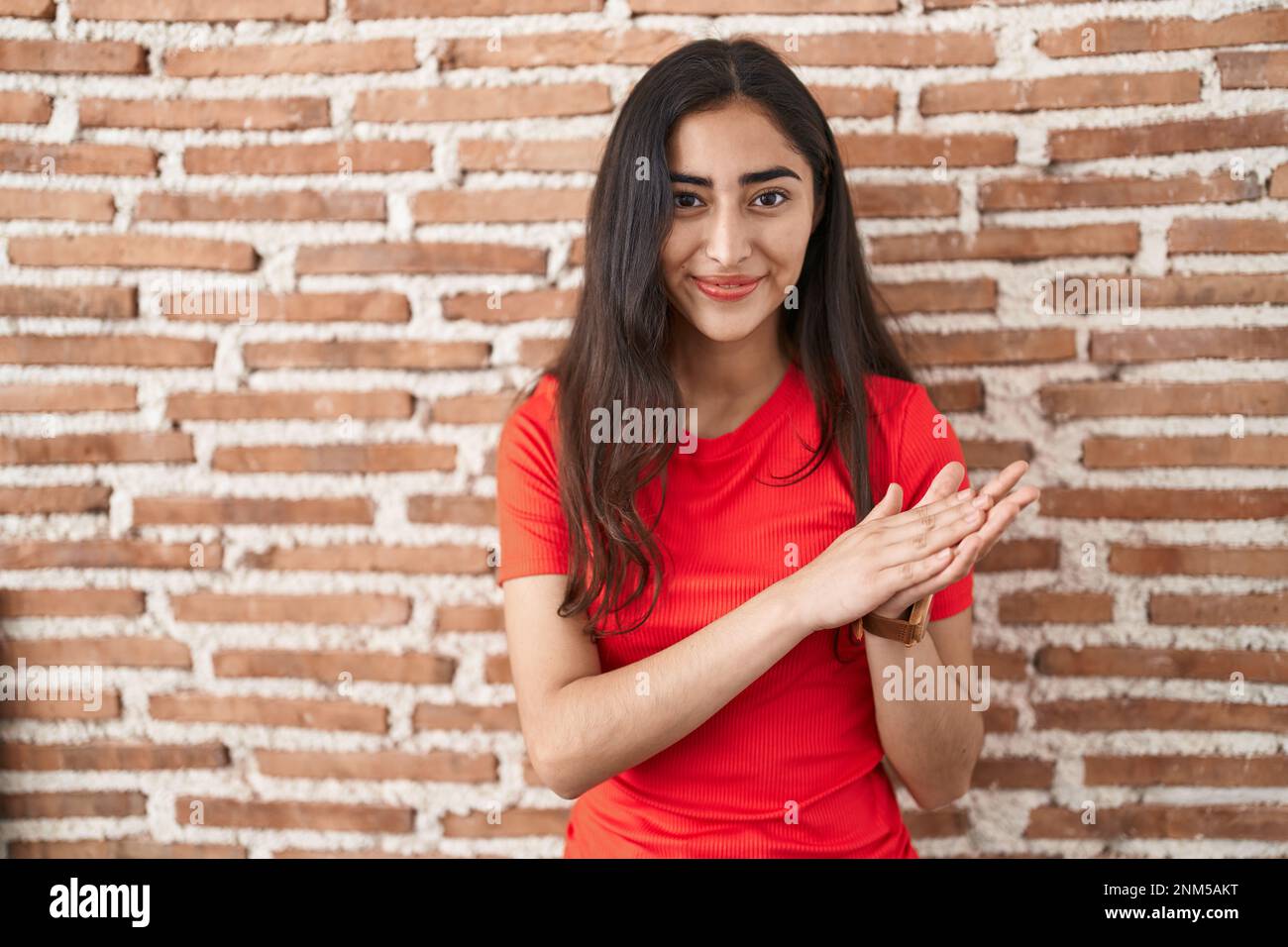 Young teenager girl standing over bricks wall clapping and applauding ...
