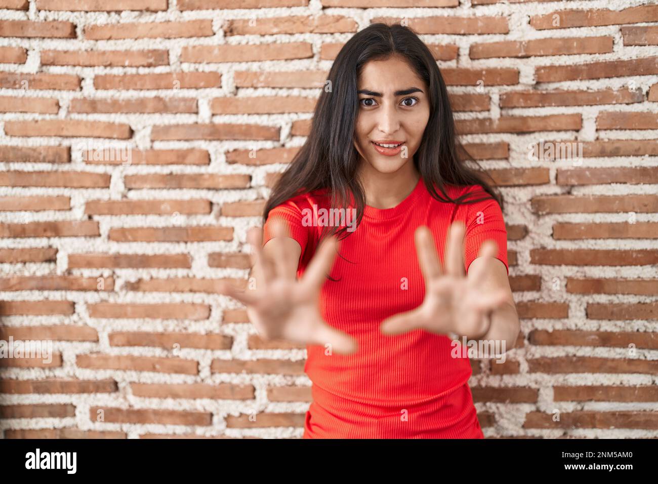 Young teenager girl standing over bricks wall afraid and terrified with ...