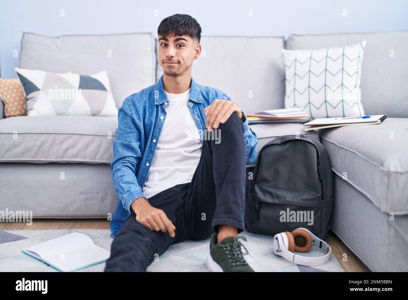 Young hispanic man sitting on the floor studying for university smiling ...