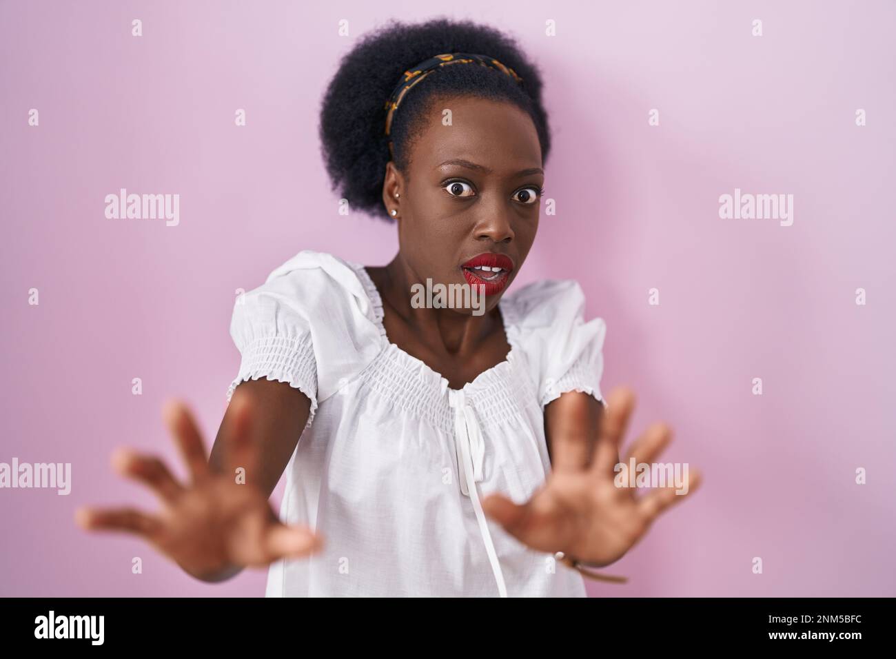 African woman with curly hair standing over pink background afraid and ...