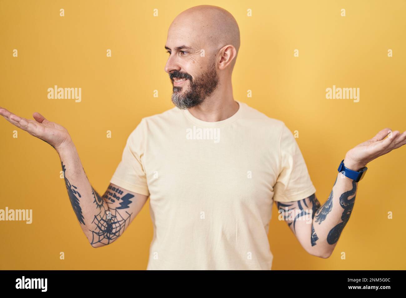 Hispanic man with tattoos standing over yellow background smiling ...