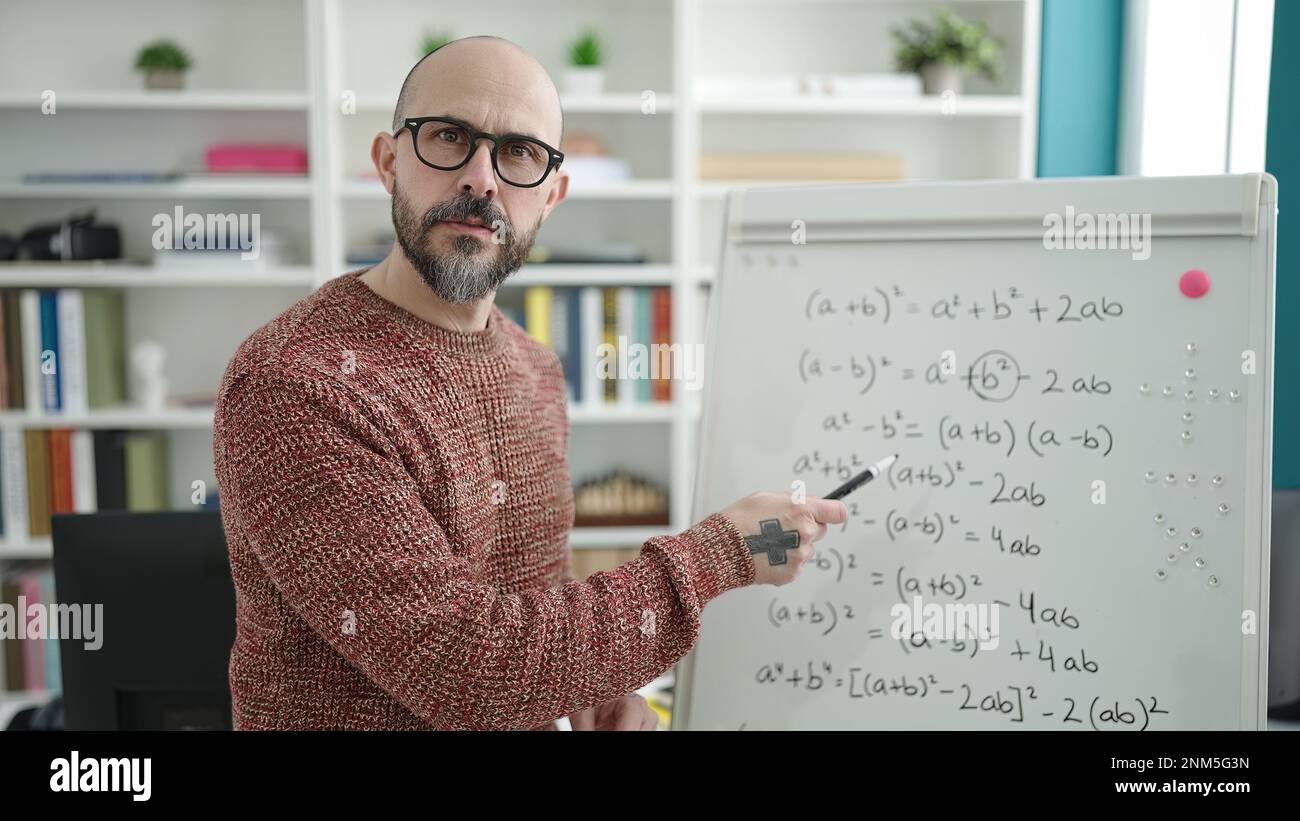 Young bald man teacher teaching maths on magnetic board at university ...