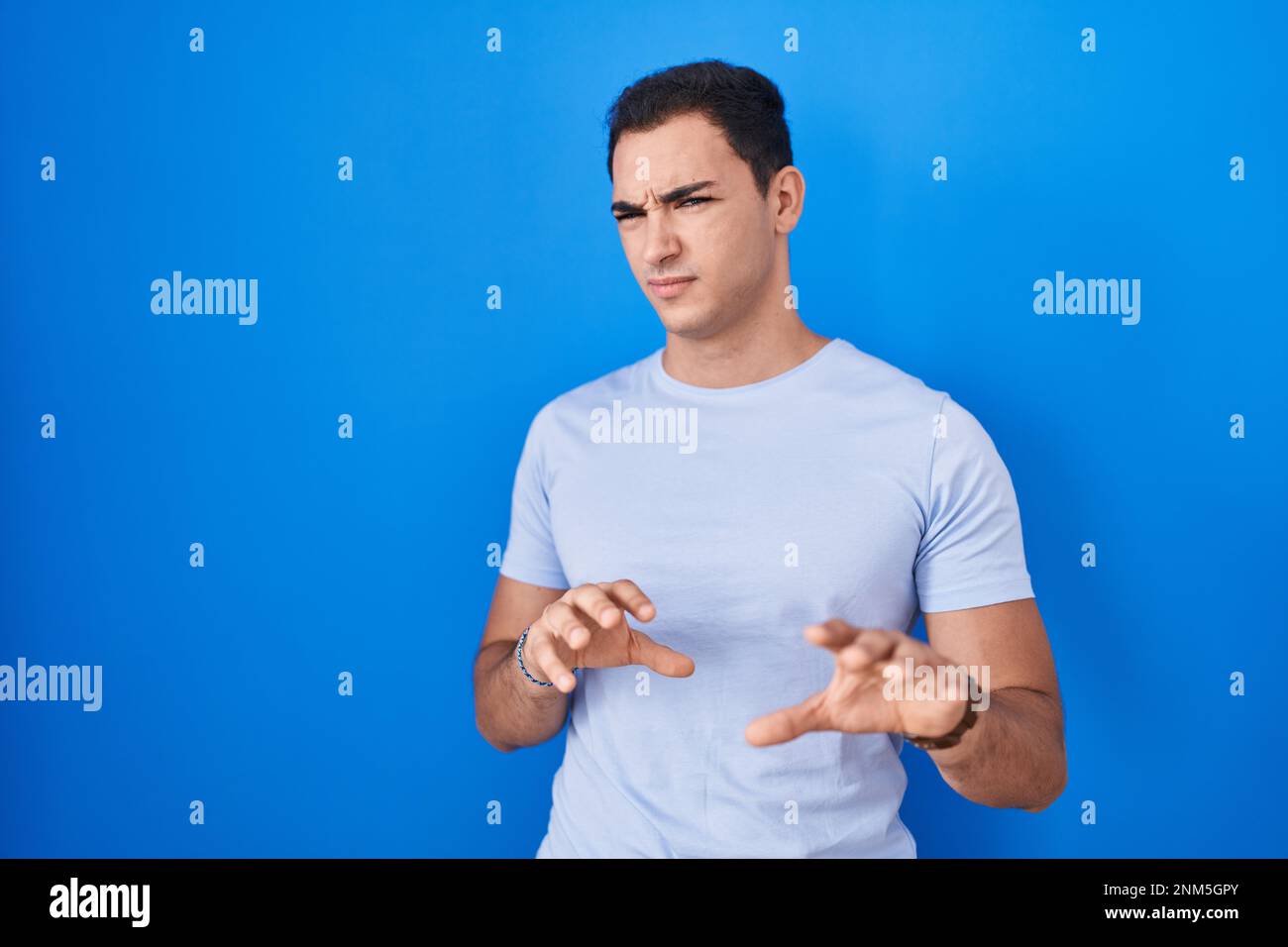Young hispanic man standing over blue background disgusted expression ...