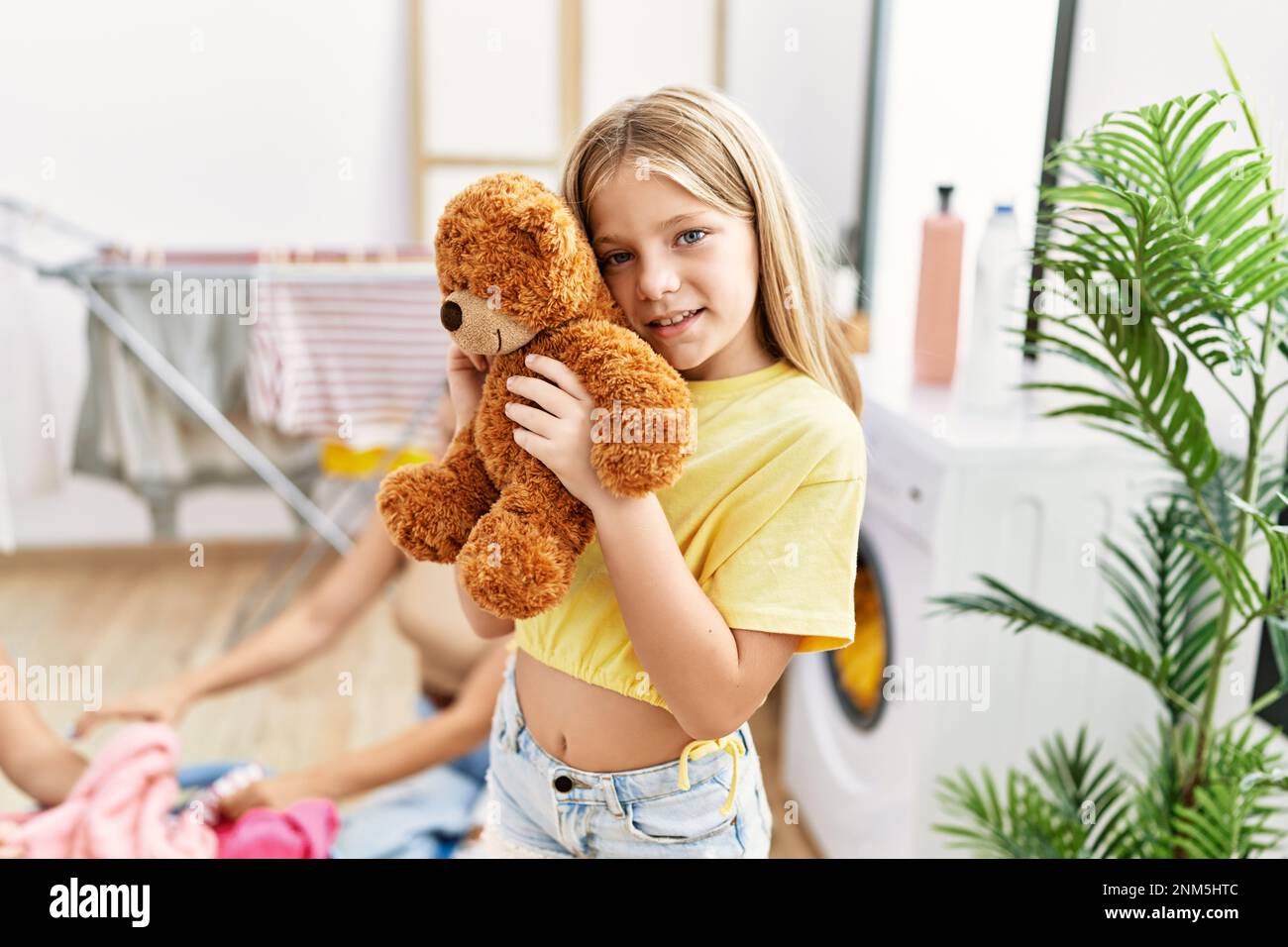 Mother and daughters holding soft teddy bear washing clothes at laundry room Stock Photo - Alamy