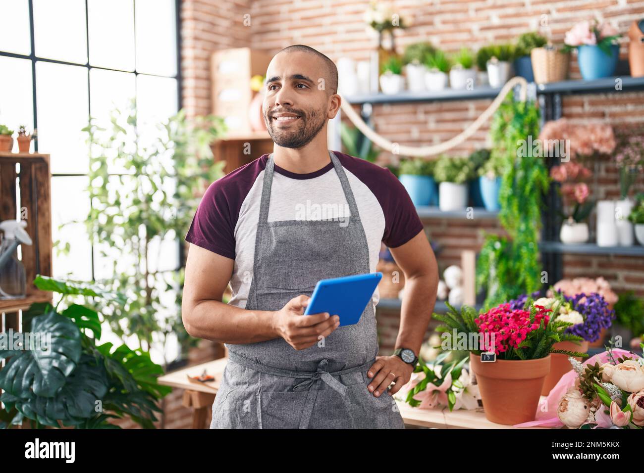 Young latin man florist smiling confident using touchpad at flower shop ...