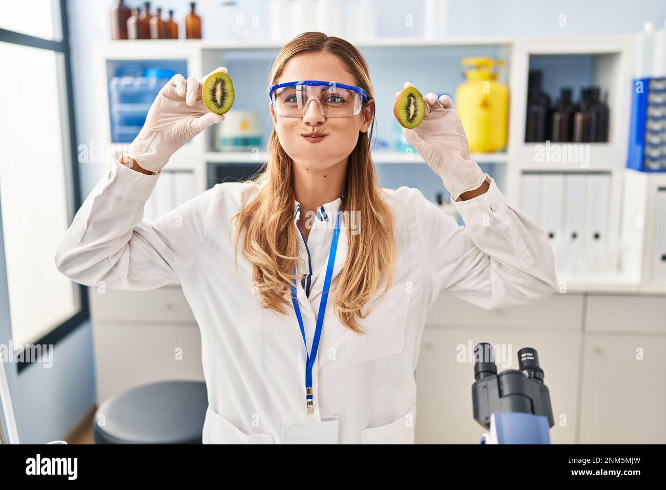 Young blonde scientist woman working with food at laboratory puffing ...