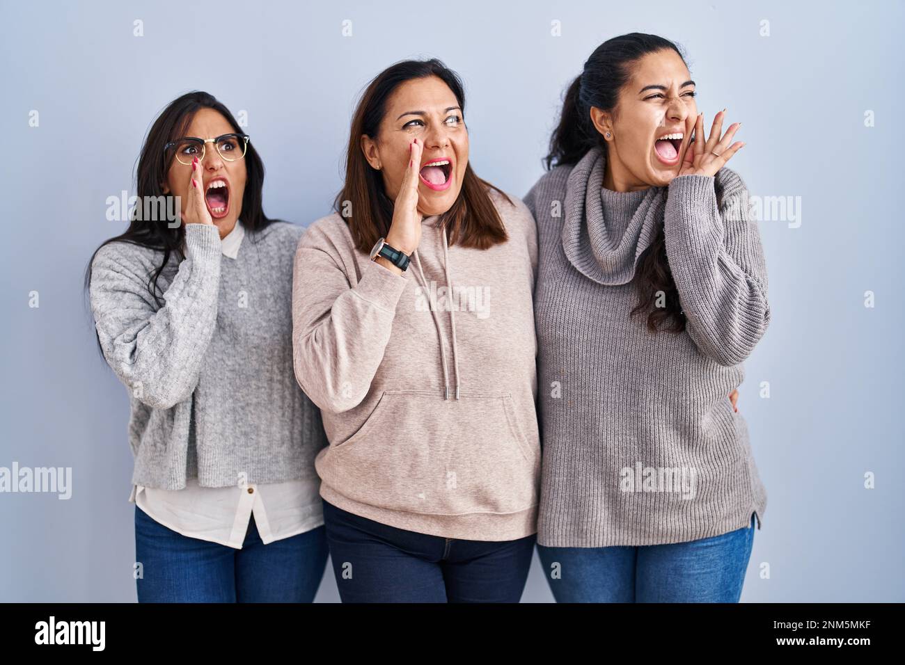 Mother and two daughters standing over blue background shouting and ...