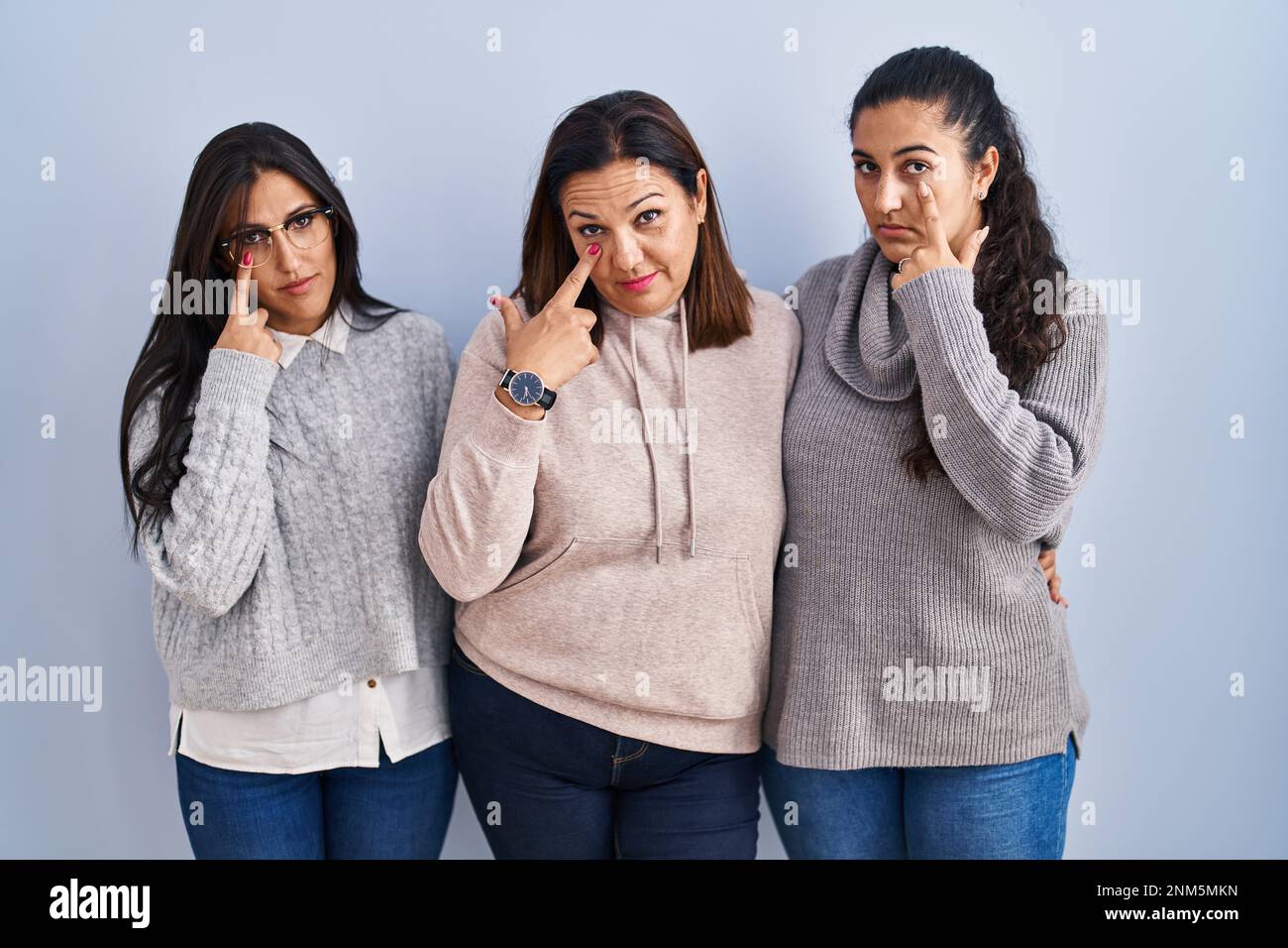 Mother and two daughters standing over blue background pointing to the ...