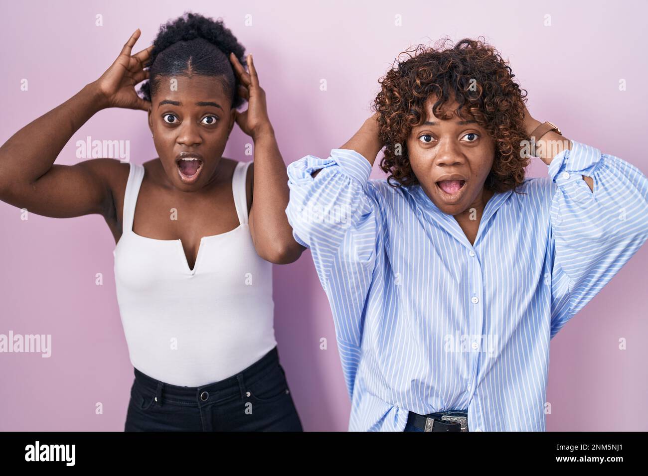 Two african women standing over pink background crazy and scared with ...