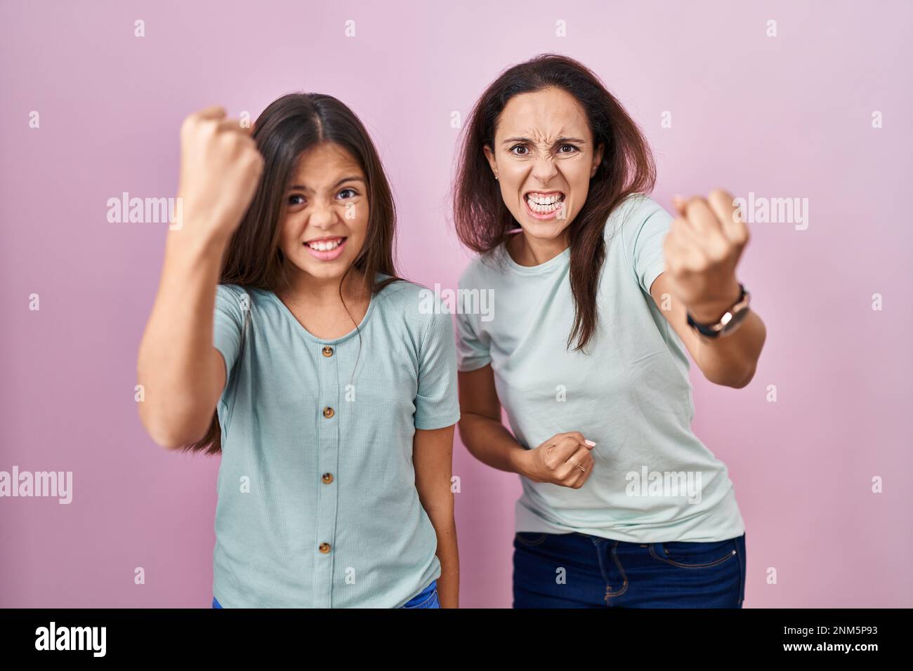 Young mother and daughter standing over pink background angry and mad ...