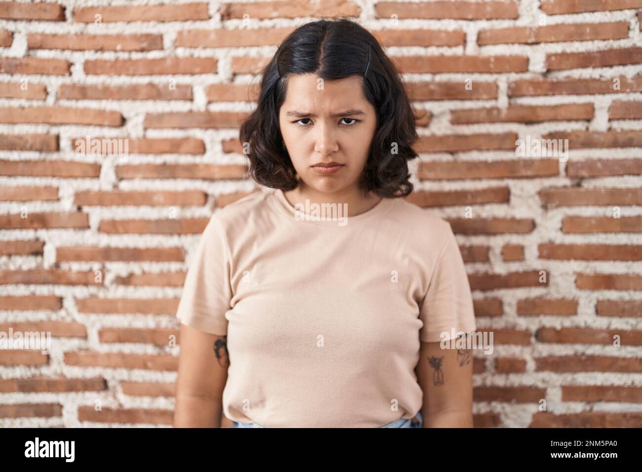 Young hispanic woman standing over bricks wall skeptic and nervous ...