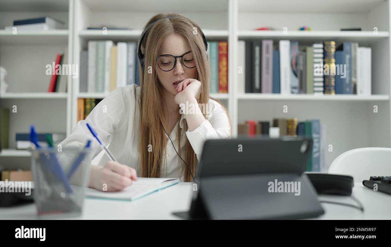 Young blonde woman student using touchpad writing on notebook at ...