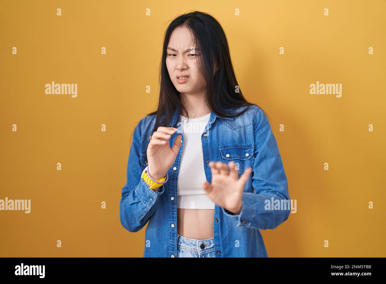 Young asian woman standing over yellow background disgusted expression ...