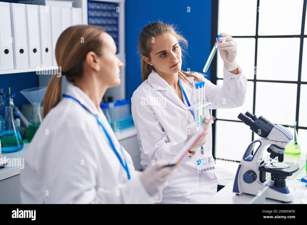 Two women scientists write on document holding test tubes at laboratory ...
