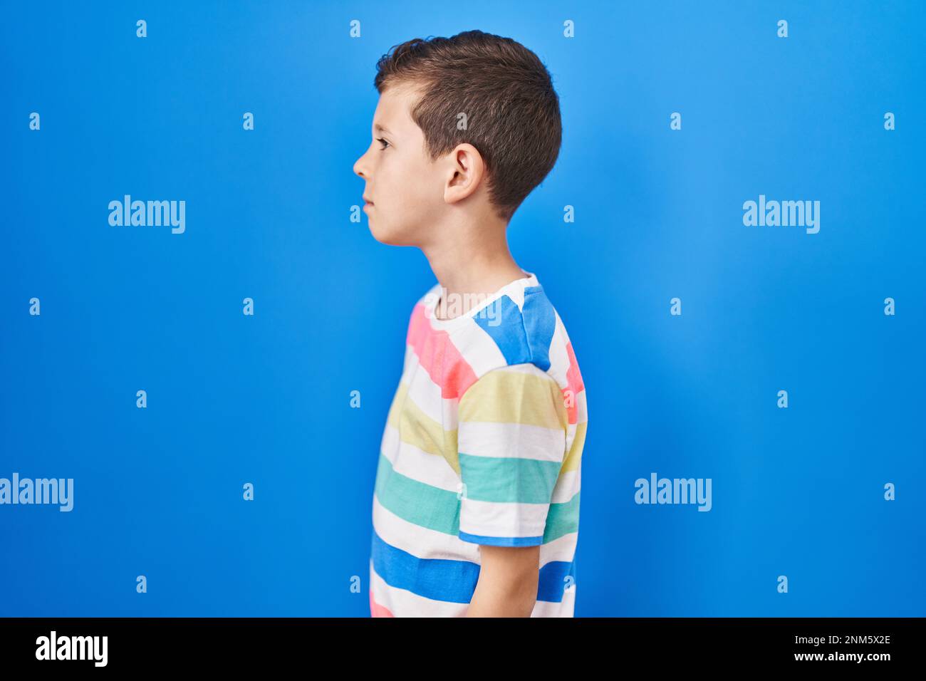 Young caucasian kid standing over blue background looking to side ...