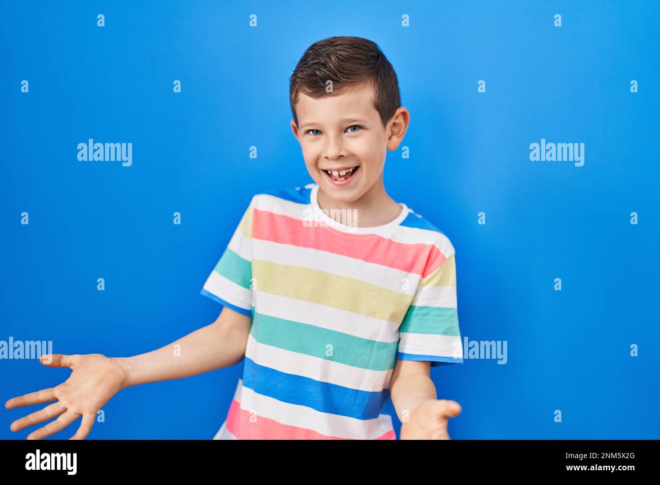Young caucasian kid standing over blue background smiling cheerful with ...