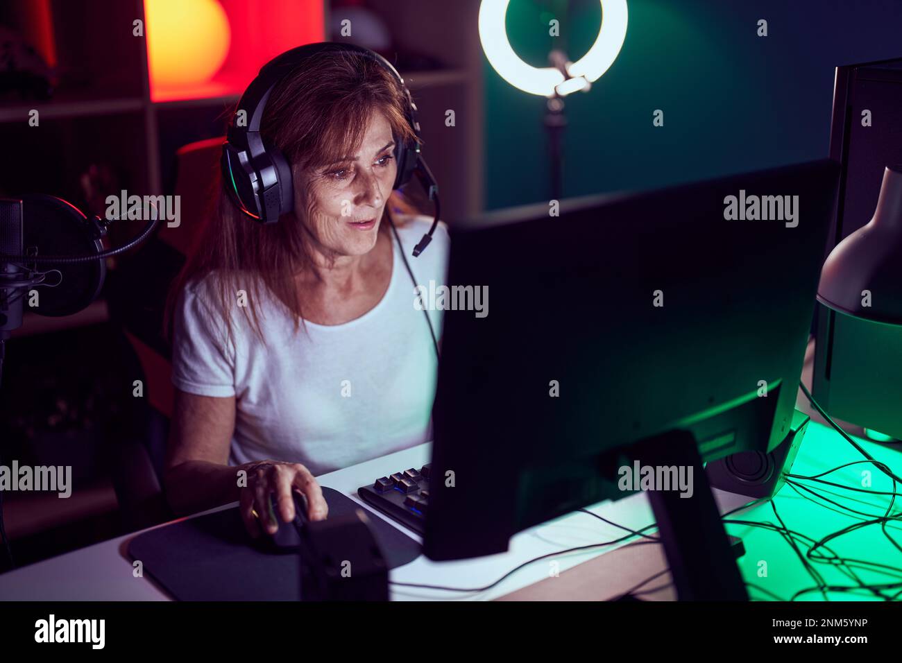 Middle age woman streamer playing video game using computer at gaming ...