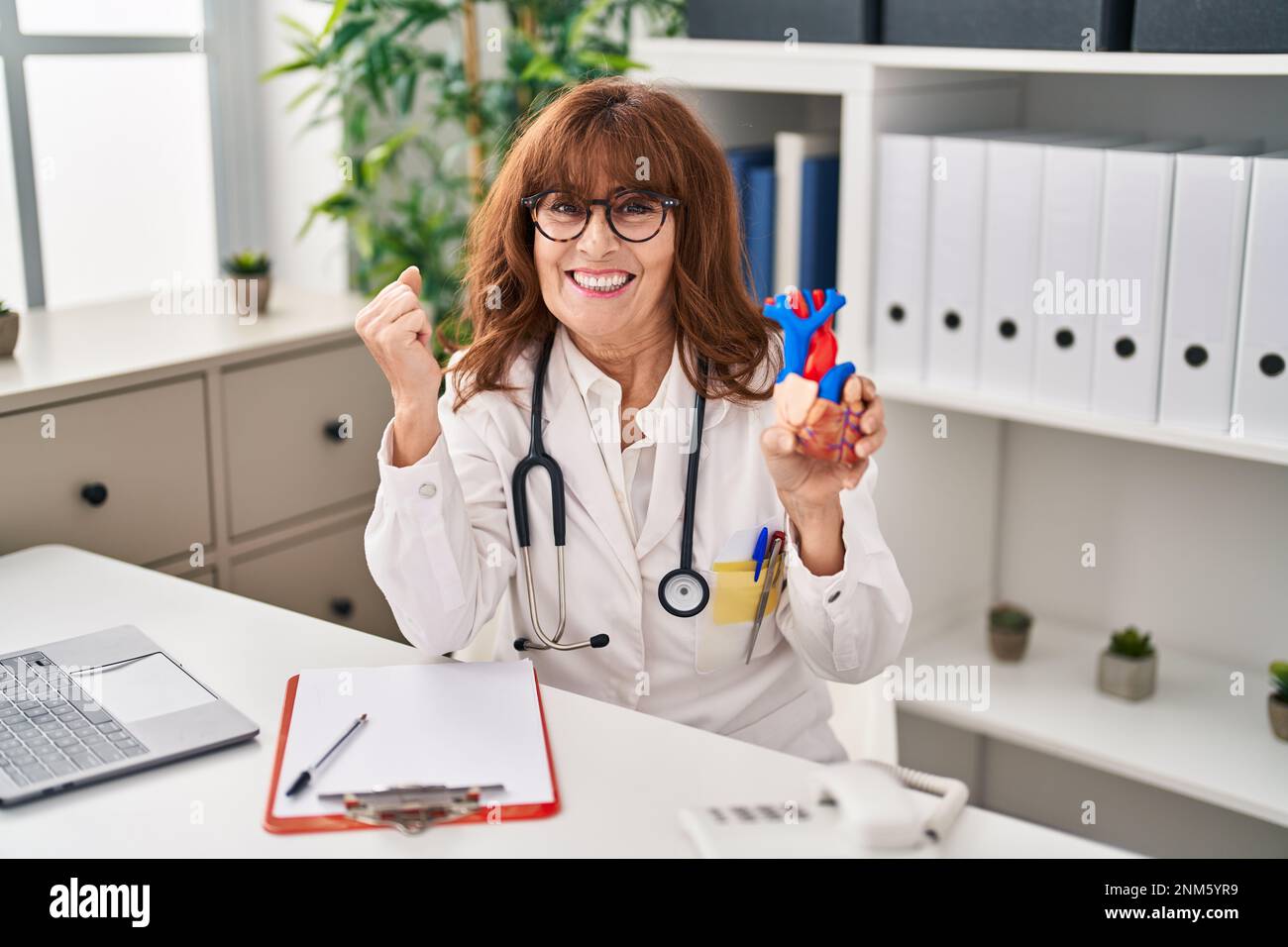 Middle age hispanic woman holding heart organ screaming proud ...