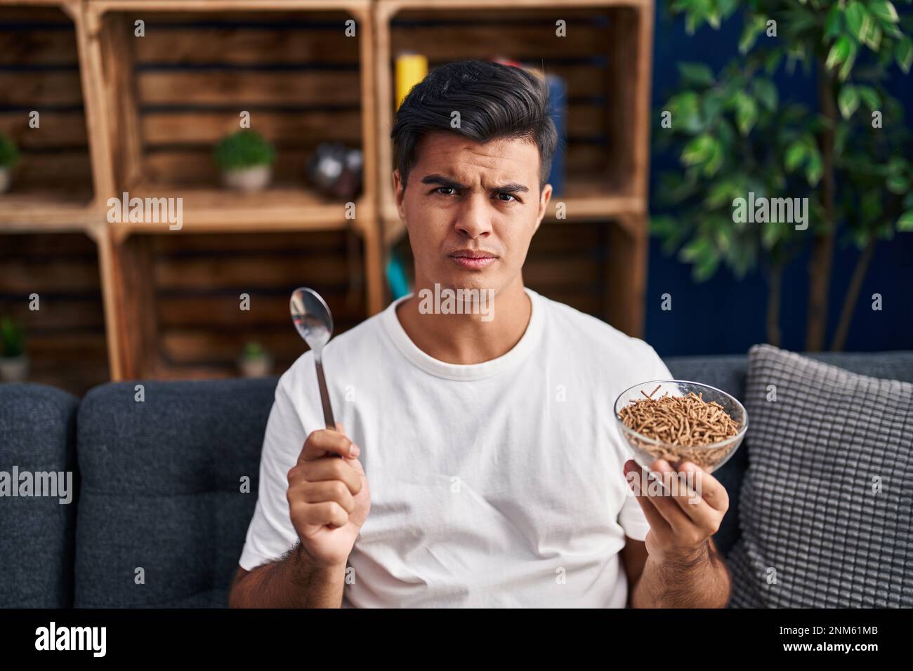 Hispanic man eating healthy whole grain cereals with spoon skeptic and ...