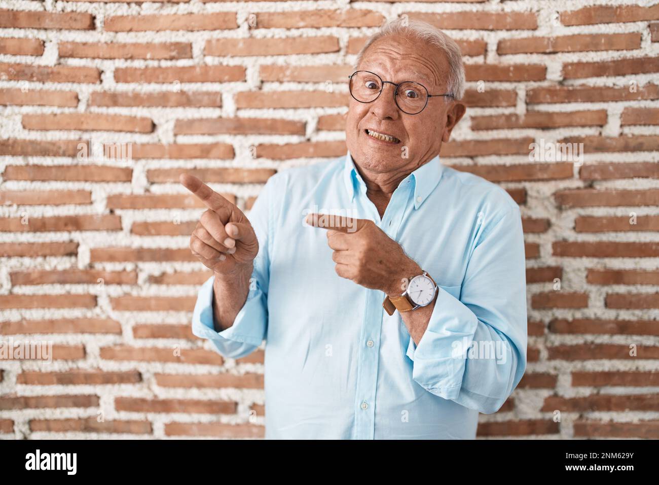 Senior man with grey hair standing over bricks wall pointing aside ...