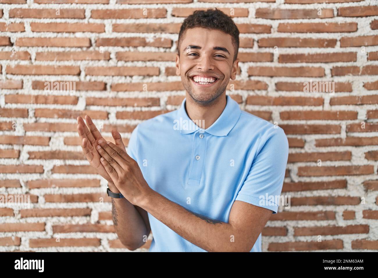 Brazilian young man standing over brick wall clapping and applauding ...