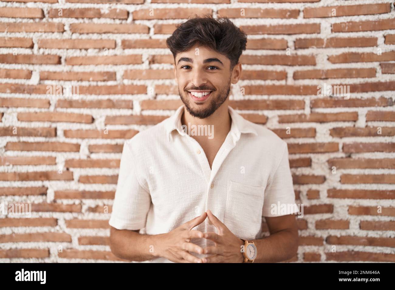 Arab man with beard standing over bricks wall background hands together ...