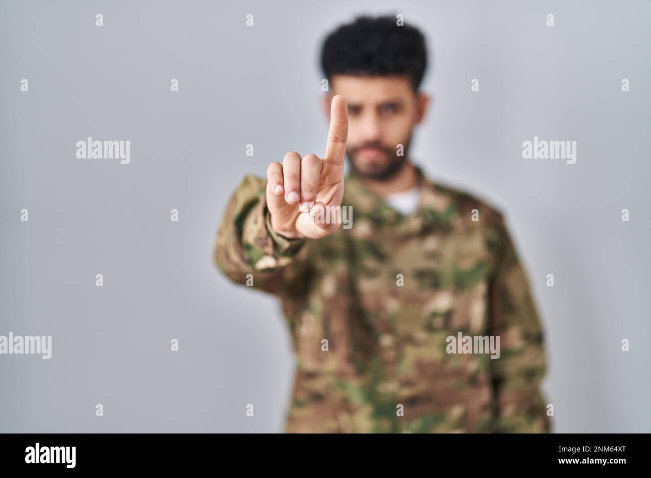 Arab man wearing camouflage army uniform pointing with finger up and ...