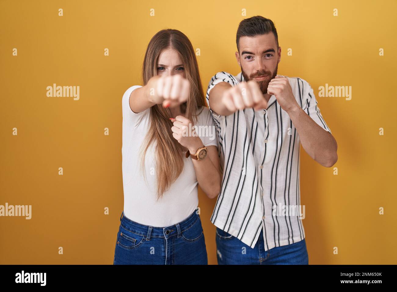 Young couple standing over yellow background punching fist to fight ...