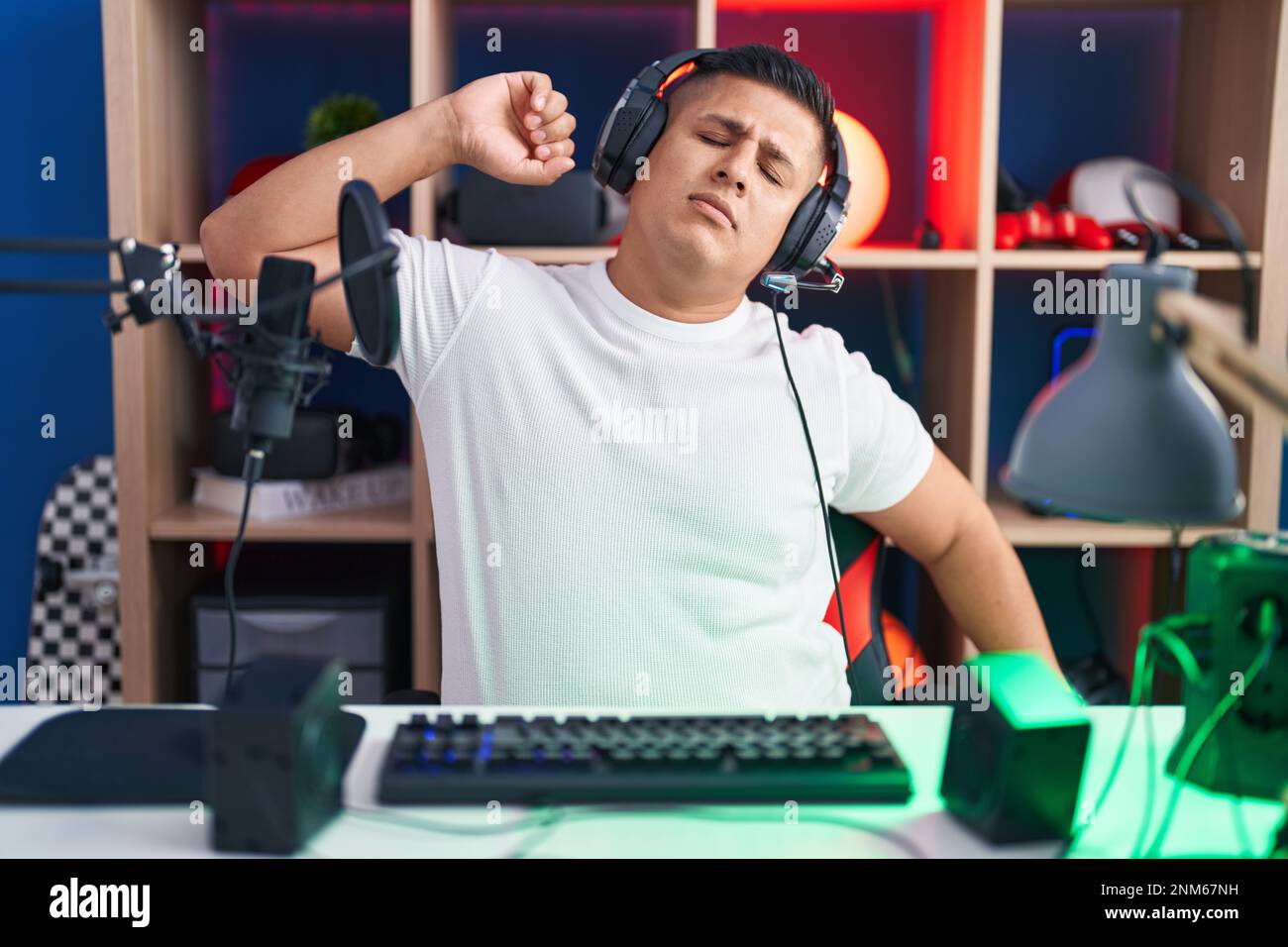 Young hispanic man playing video games stretching back, tired and ...