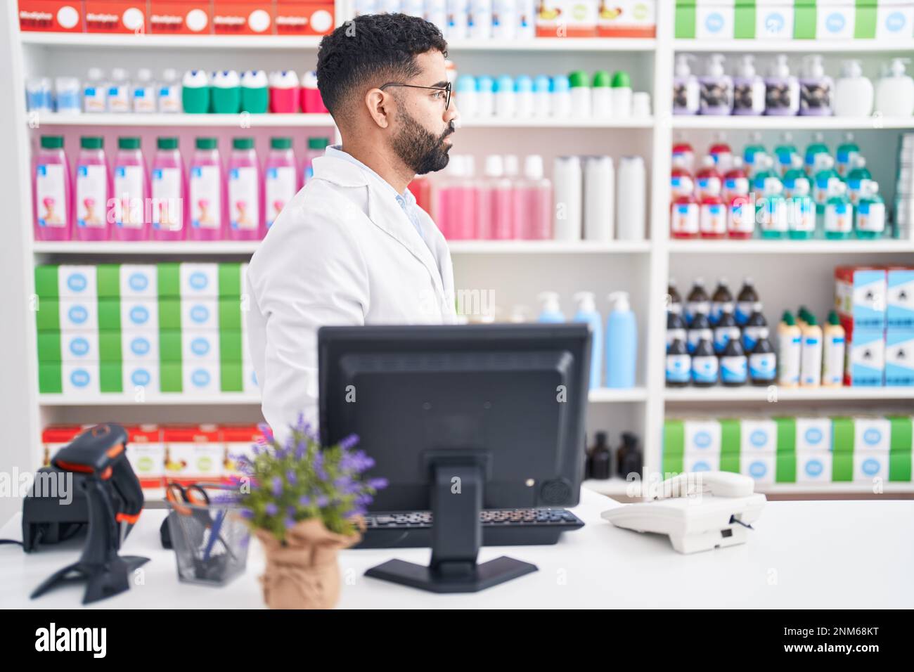 Hispanic man with beard working at pharmacy drugstore looking to side ...