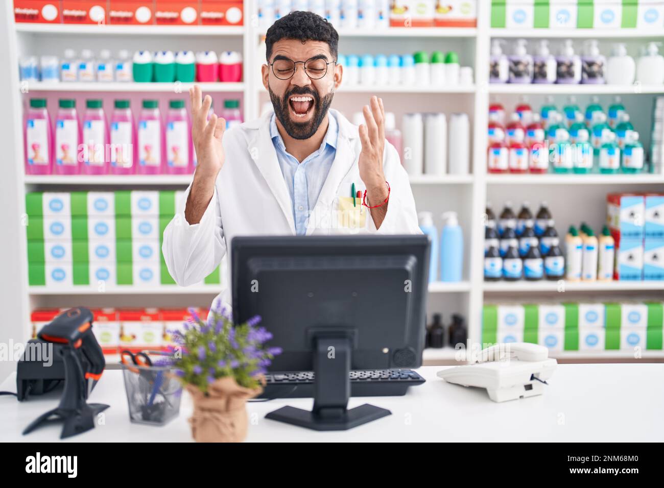 Hispanic man with beard working at pharmacy drugstore celebrating mad ...