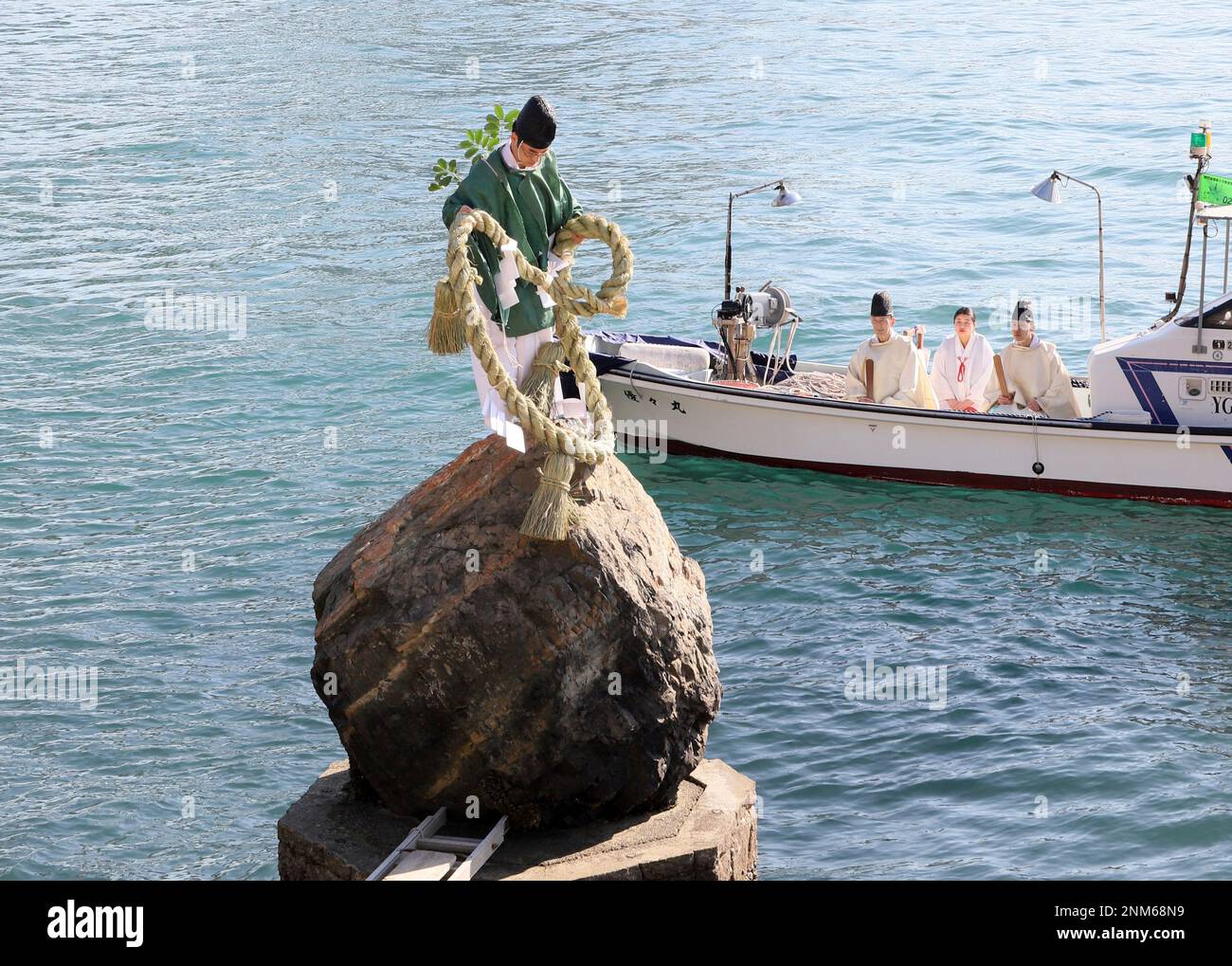 A Shinto priest, standing on a Eboshi rock, ties a sacred rope for ...