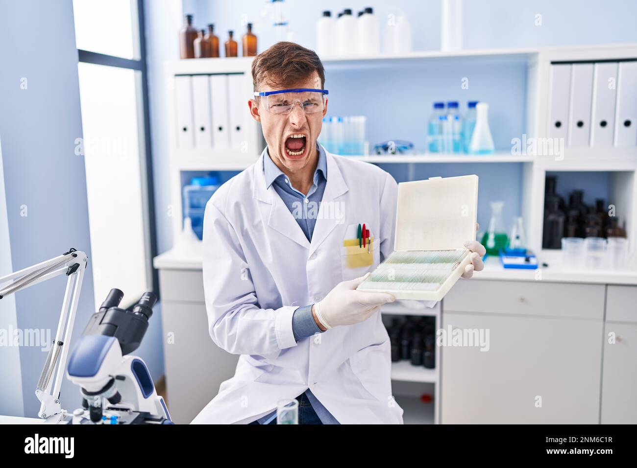 Caucasian man working at scientist laboratory angry and mad screaming ...
