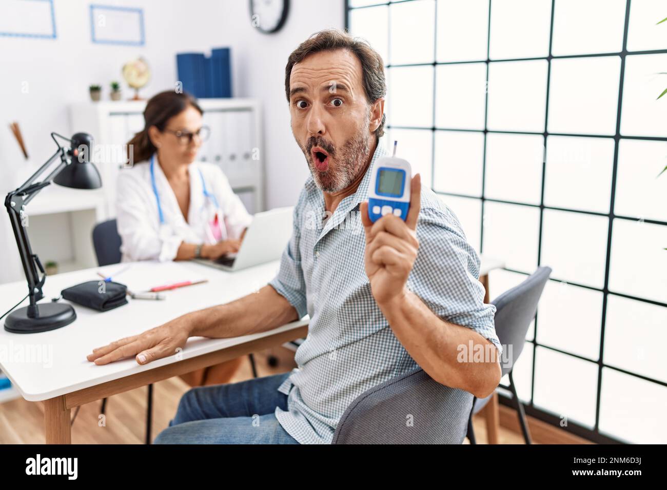Middle age man at doctor clinic holding glucose meter device scared and ...