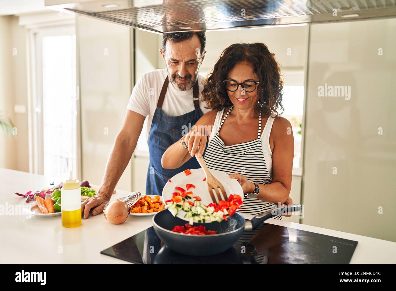 Middle age hispanic couple smiling confident pouring food on frying pan ...