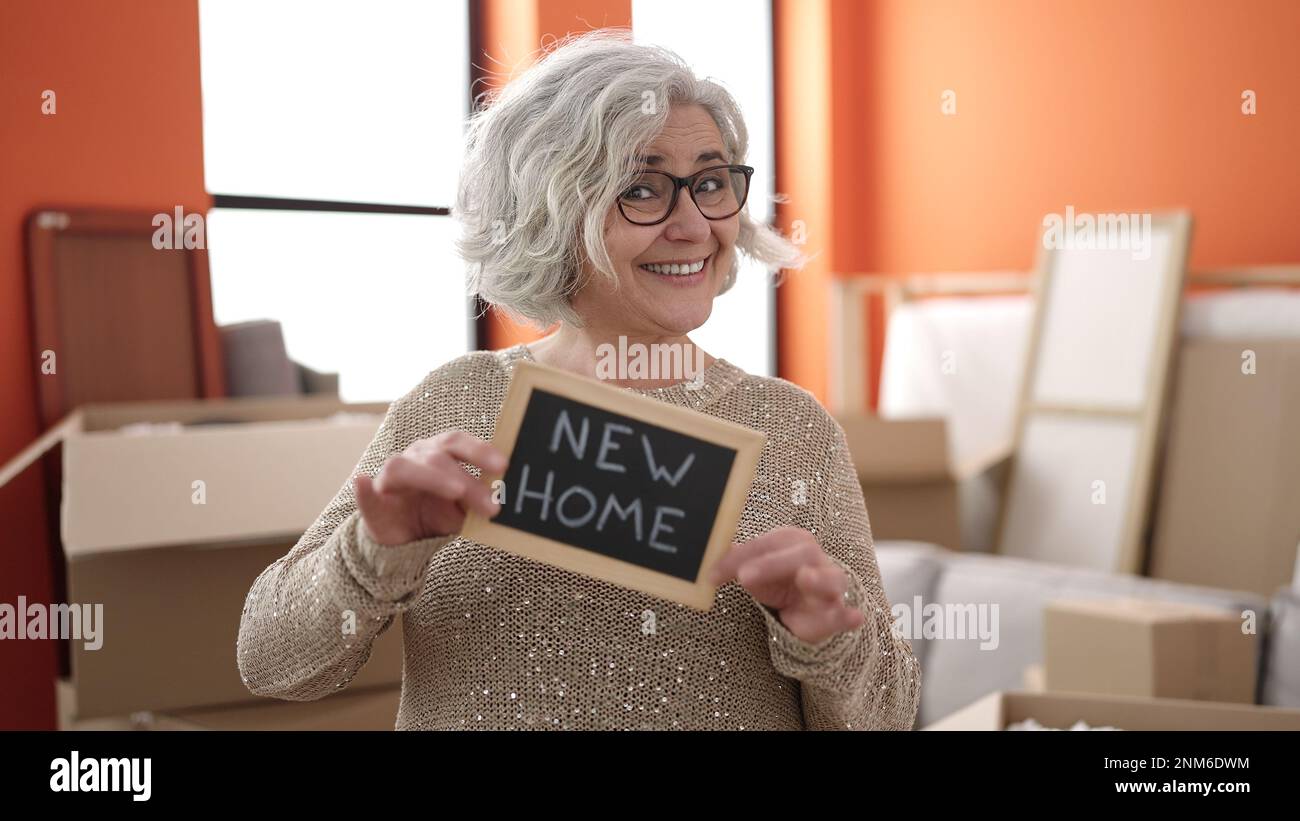 Middle age woman with grey hair holding blackboard standing at new home ...