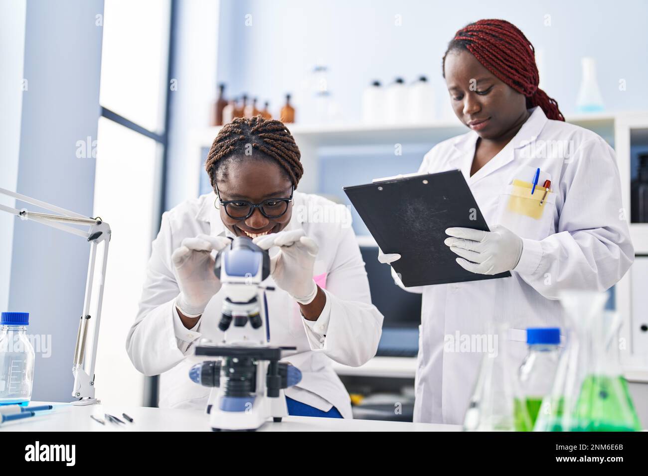 African american women scientists using microscope writing on document at laboratory Stock Photo ...
