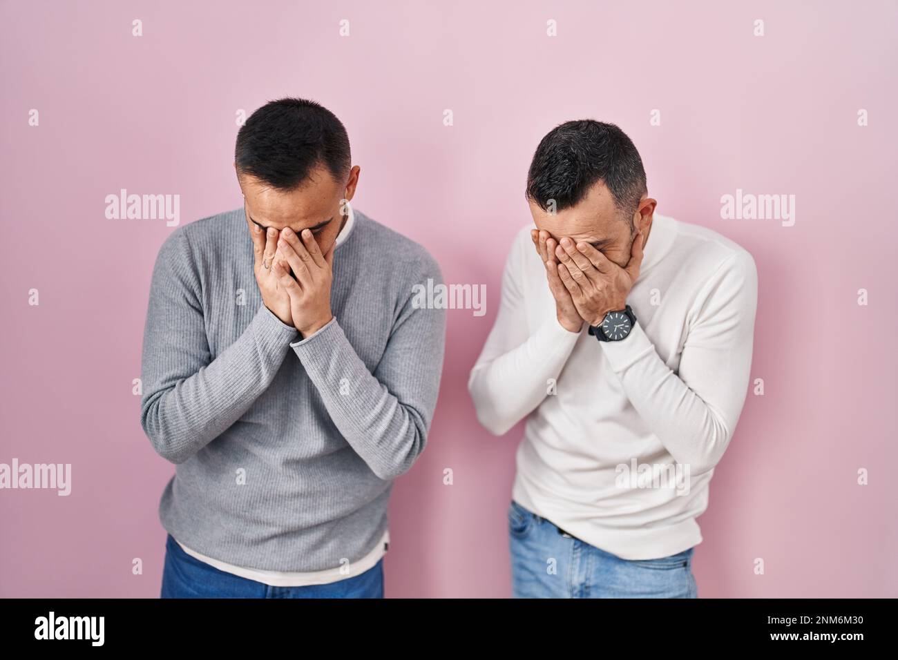 Homosexual couple standing over pink background with sad expression ...