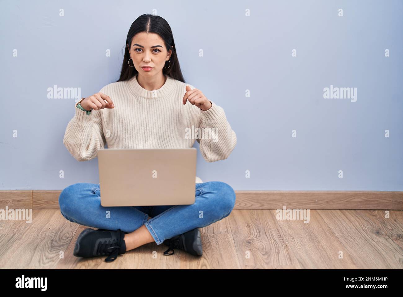 Young woman using laptop sitting on the floor at home pointing down ...