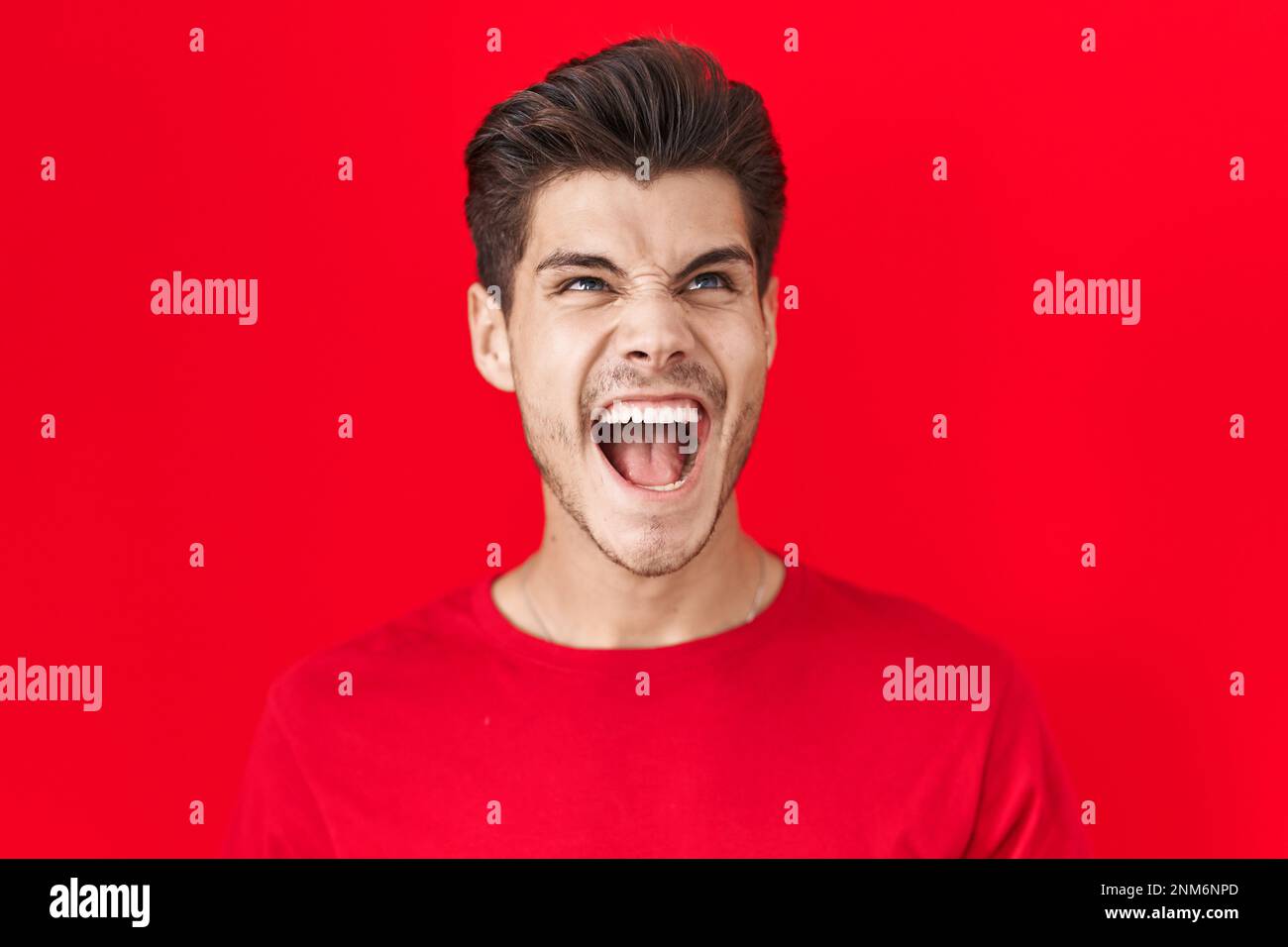 Young hispanic man standing over red background angry and mad screaming ...