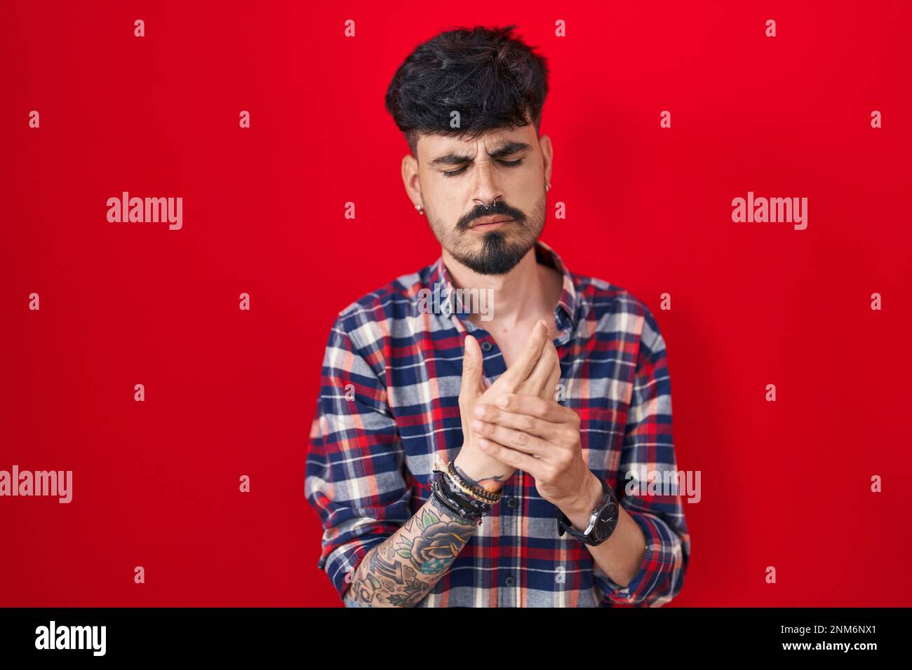 Young hispanic man with beard standing over red background suffering ...