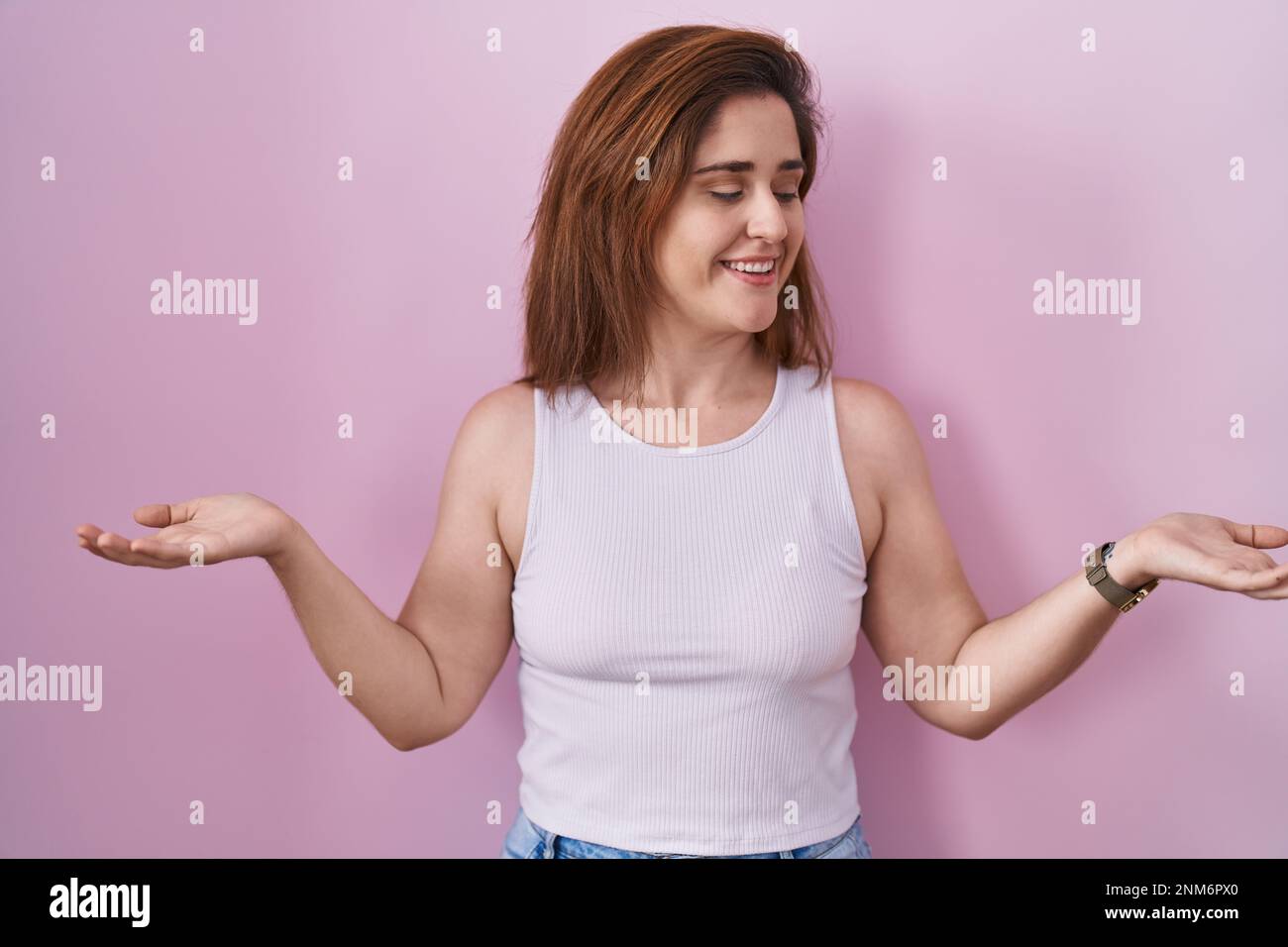 Brunette woman standing over pink background smiling showing both hands ...